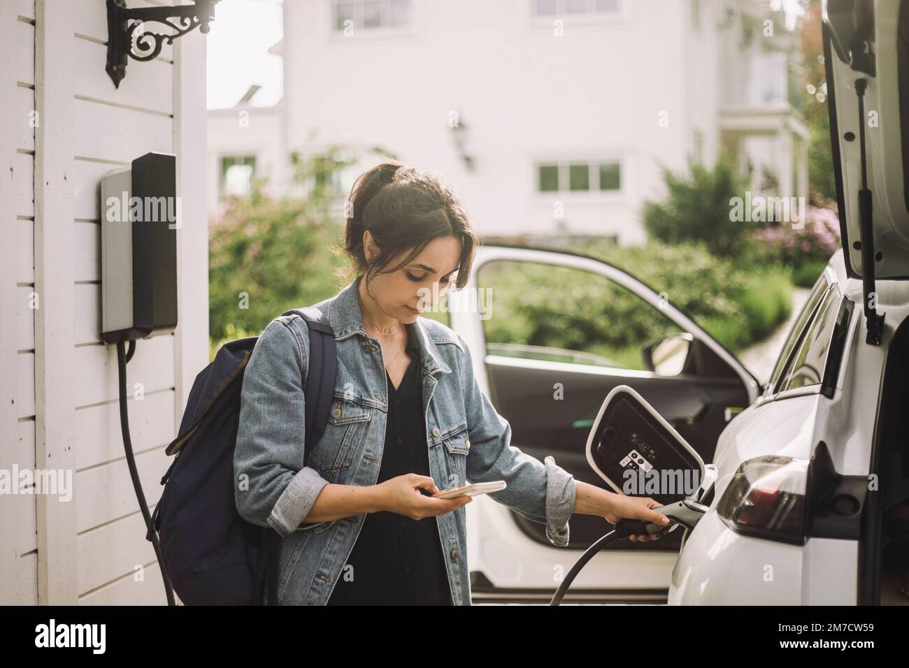 Woman charging electric car while using smart phone Stock Photo - Alamy