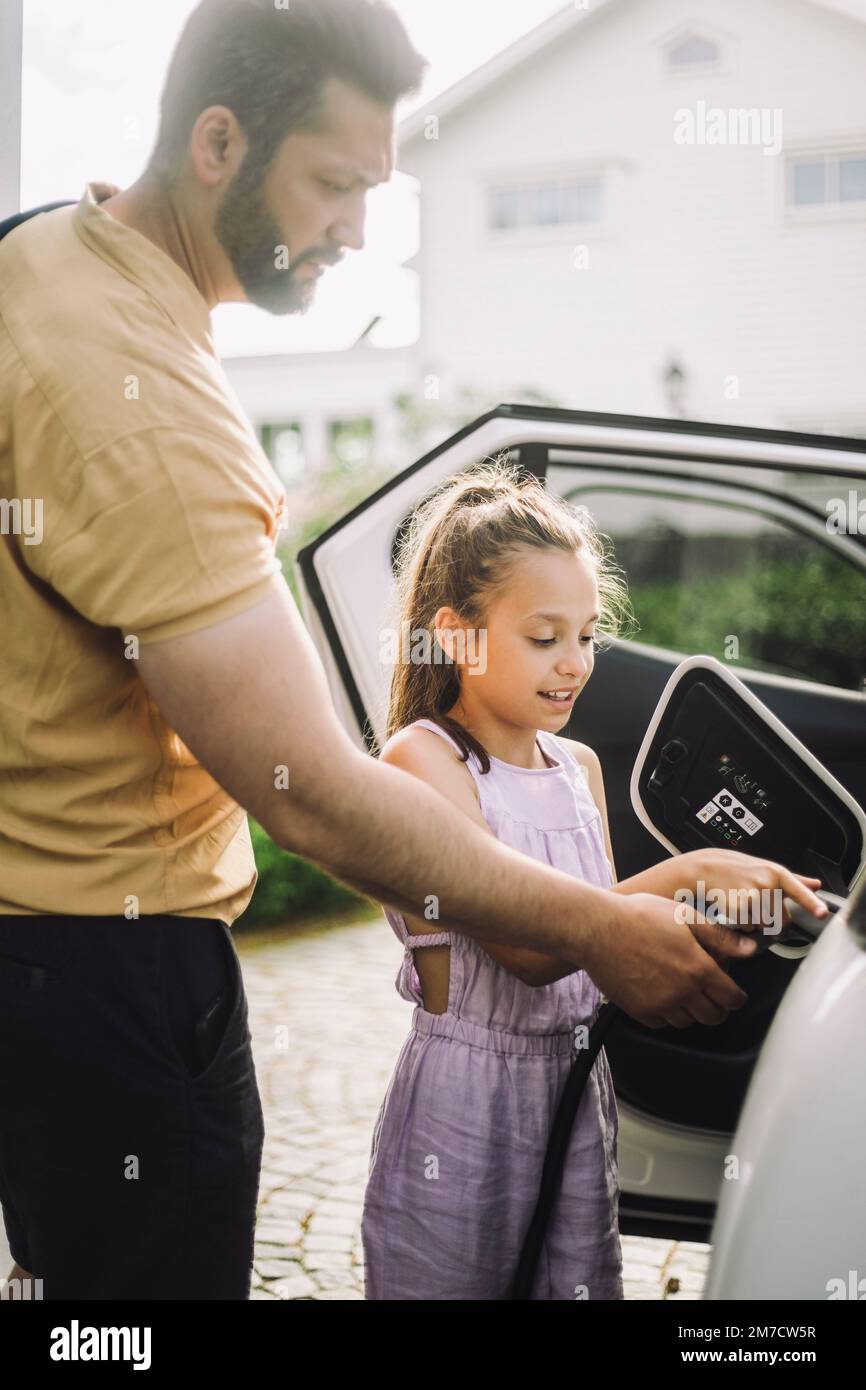 Girl learning to charge electric car while standing by father Stock ...