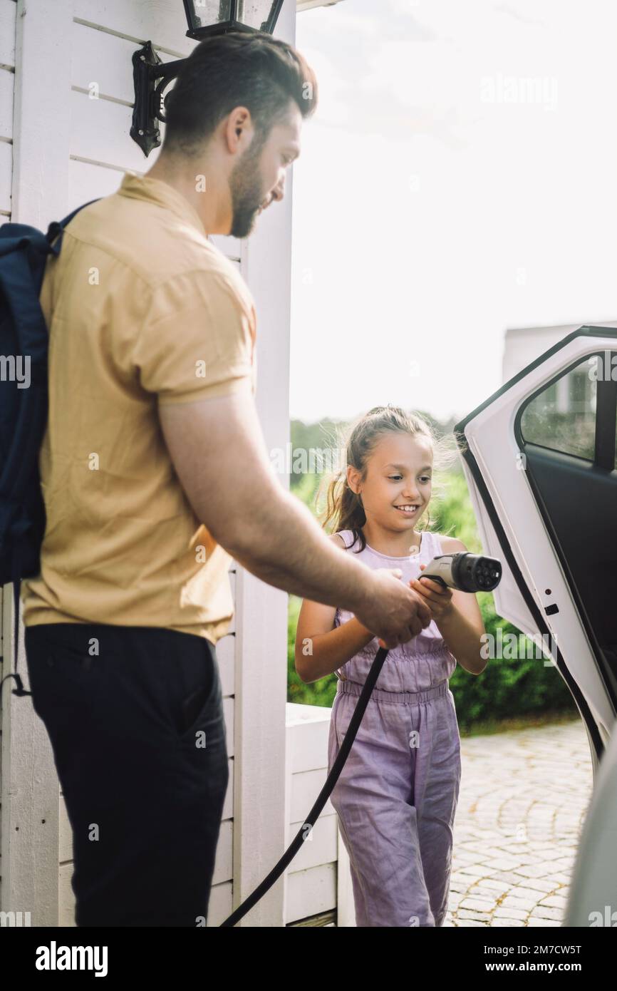 Side view of father teaching daughter to charge electric car Stock ...