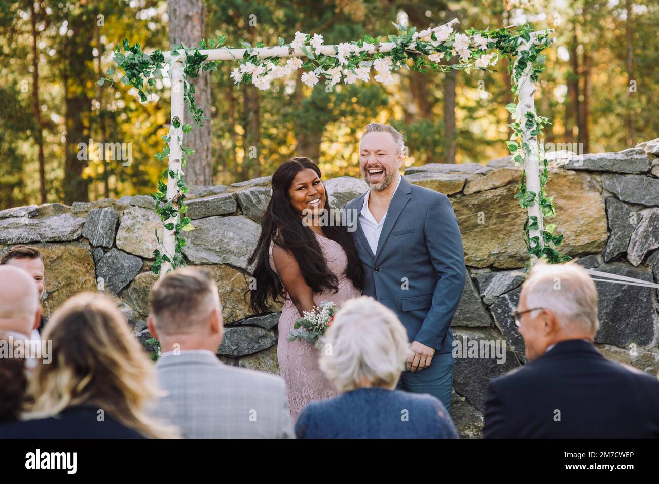Happy newlywed multiracial couple looking at guest during wedding ...