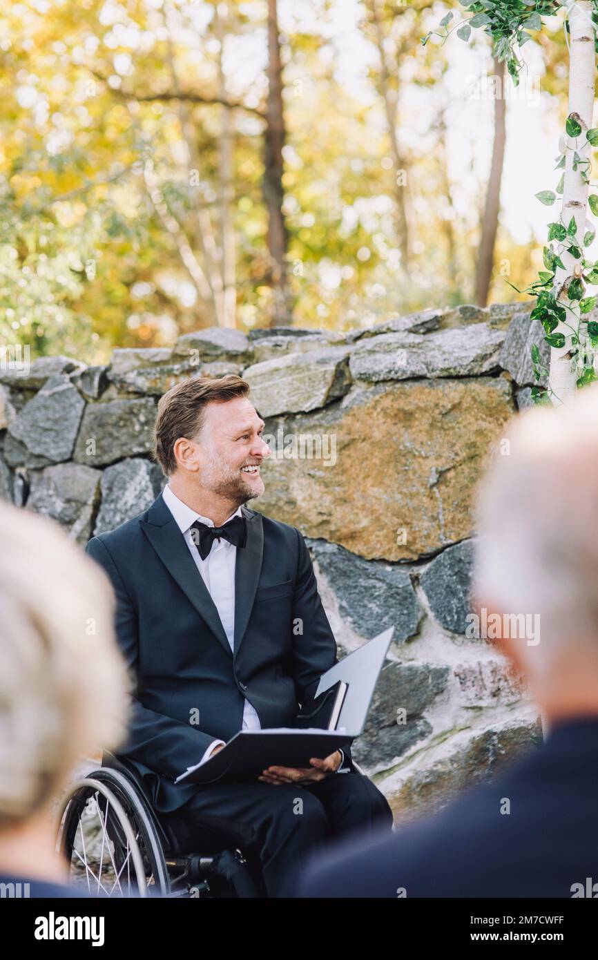 Happy minister in wheelchair with disability holding book against wall ...