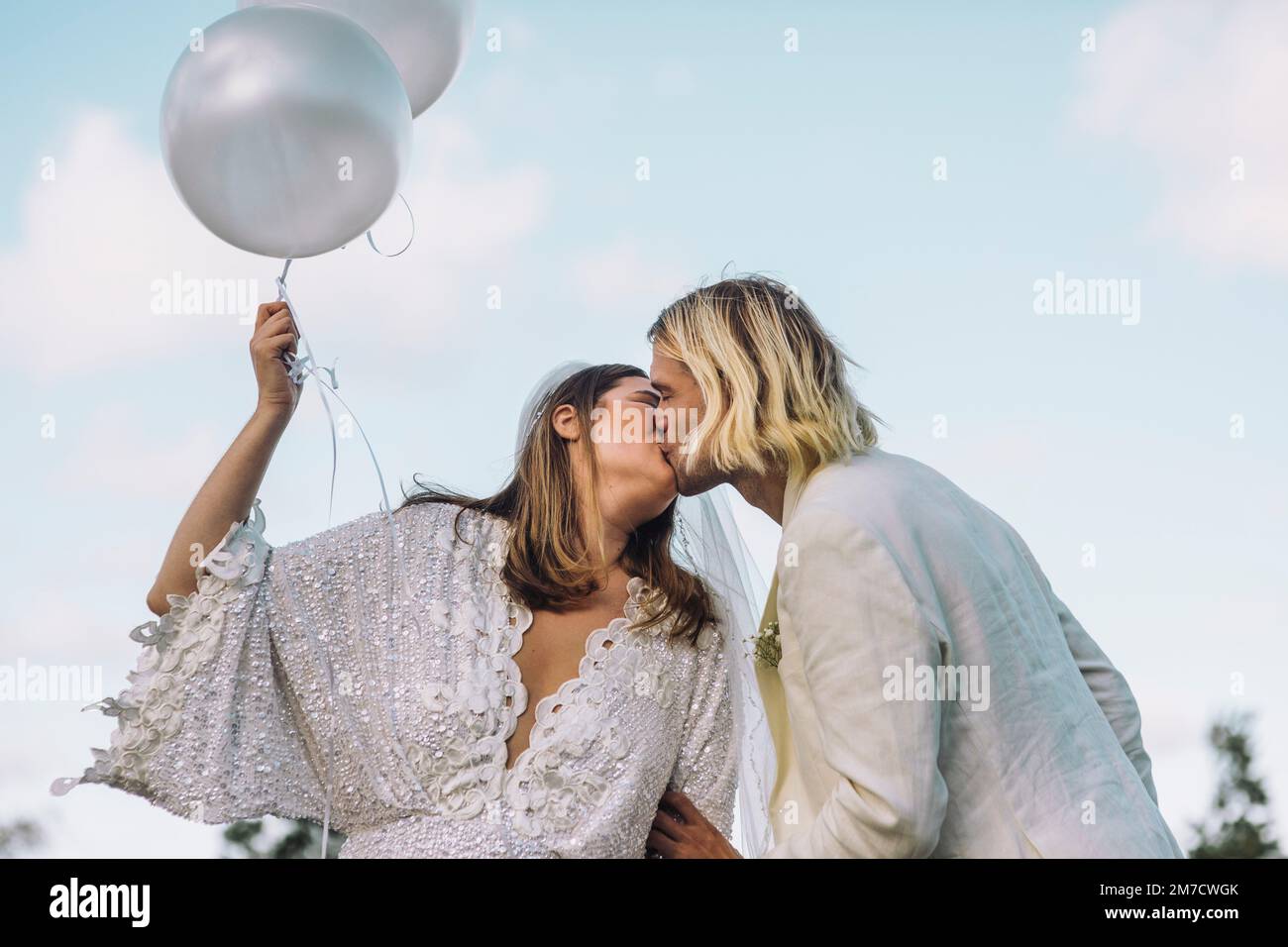 Bride holding white helium balloons kissing groom against sky Stock ...