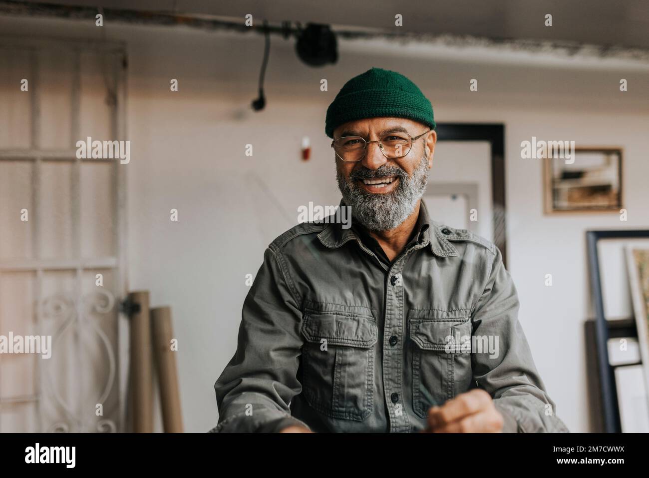 Portrait of cheerful male owner wearing knit hat and eyeglasses in ...