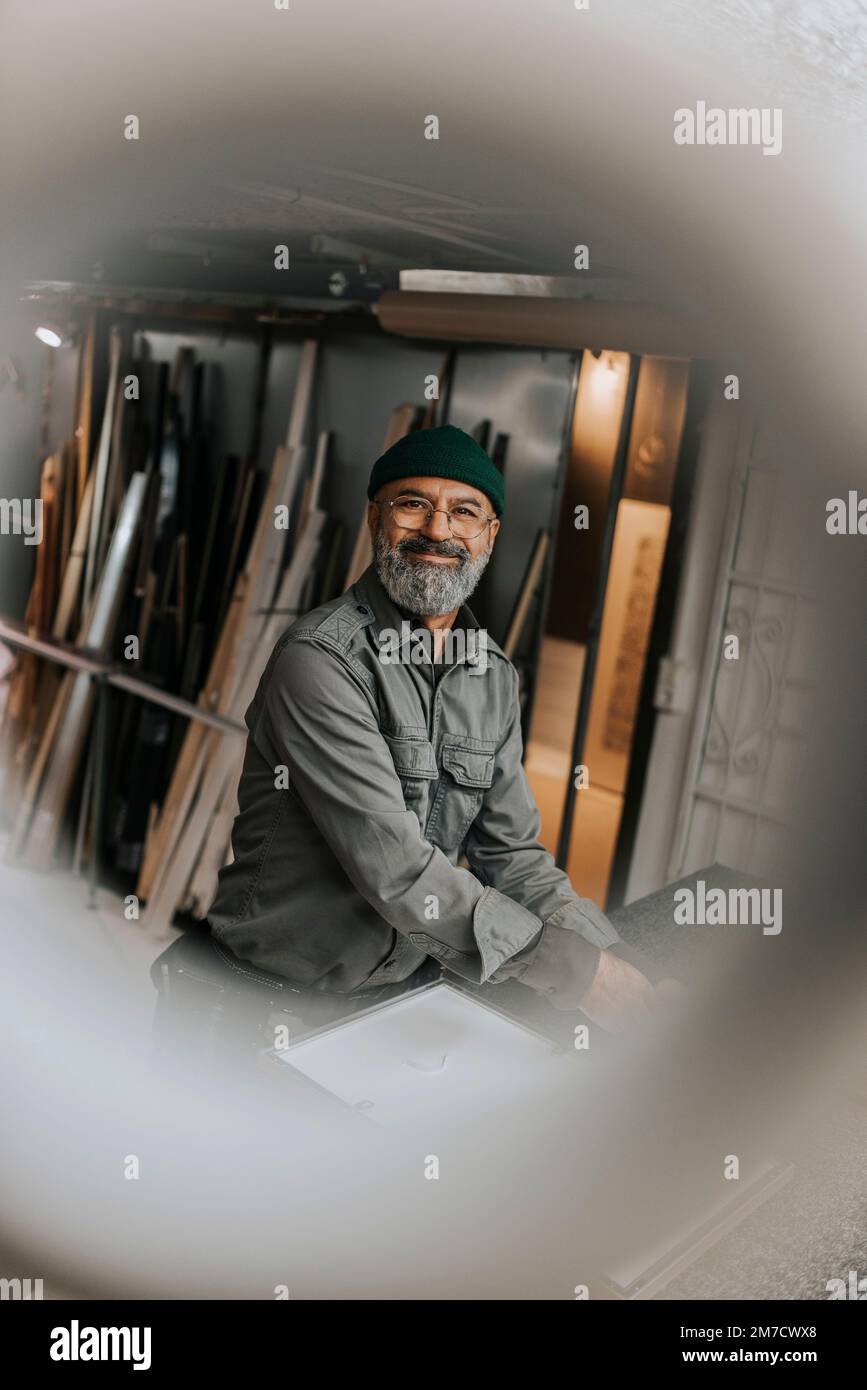 Portrait of smiling bearded craftsman wearing knit hat while standing ...