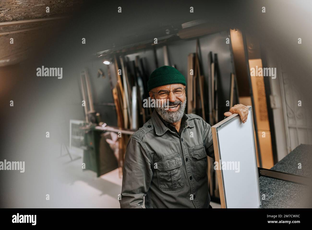 Cheerful male owner with picture frame standing at workbench Stock ...