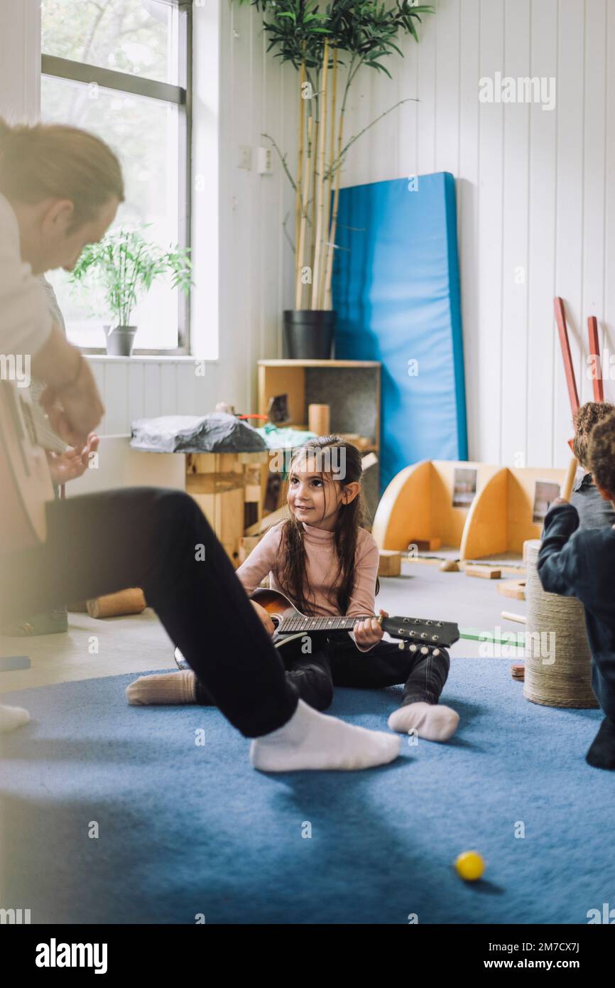 Girl learning guitar from male child care worker at kindergarten Stock ...