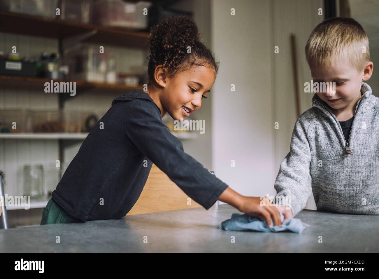 Smiling girl and boy cleaning dining table with napkin at child care ...
