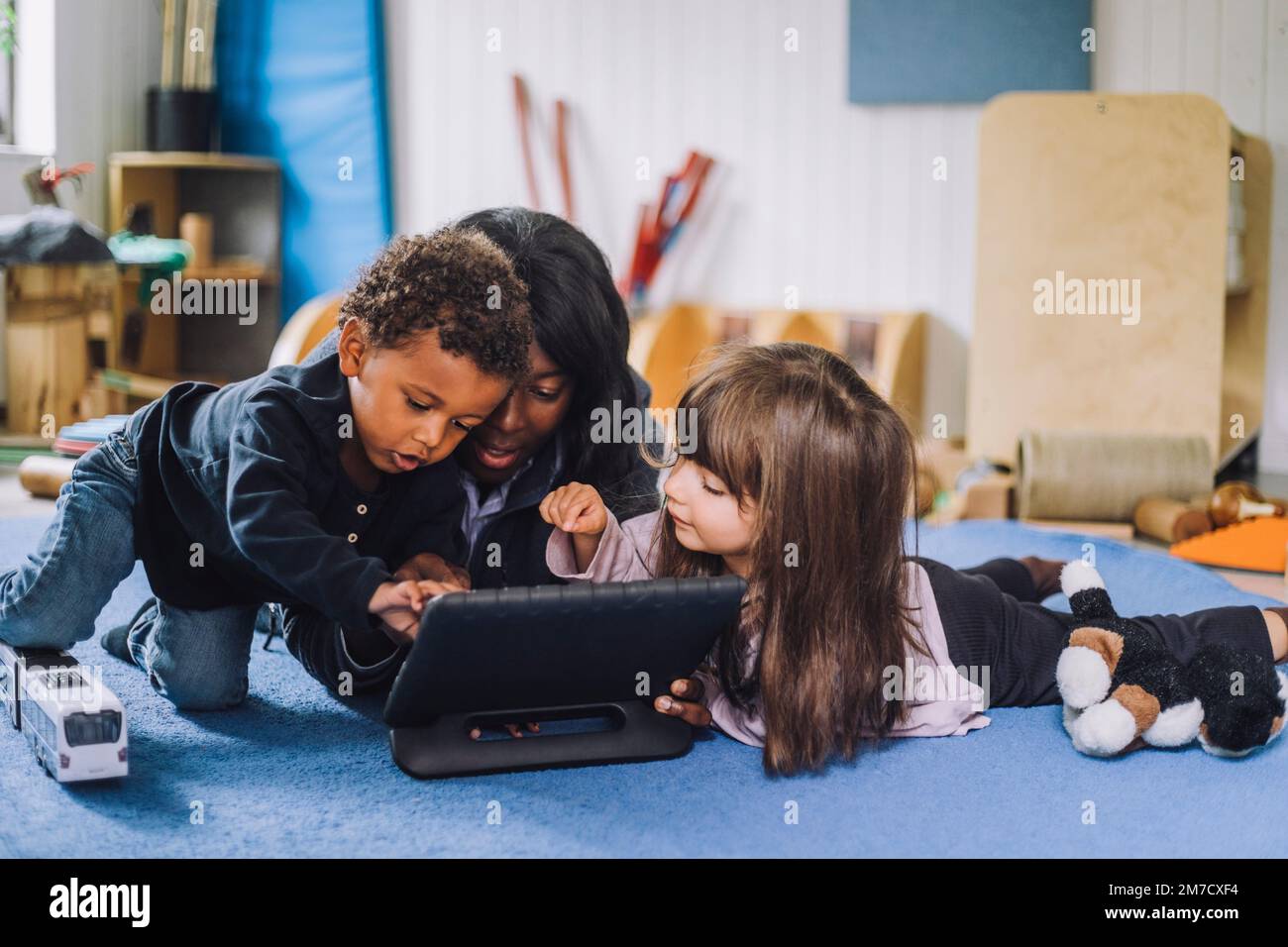Female teacher sharing digital tablet with children in child care ...