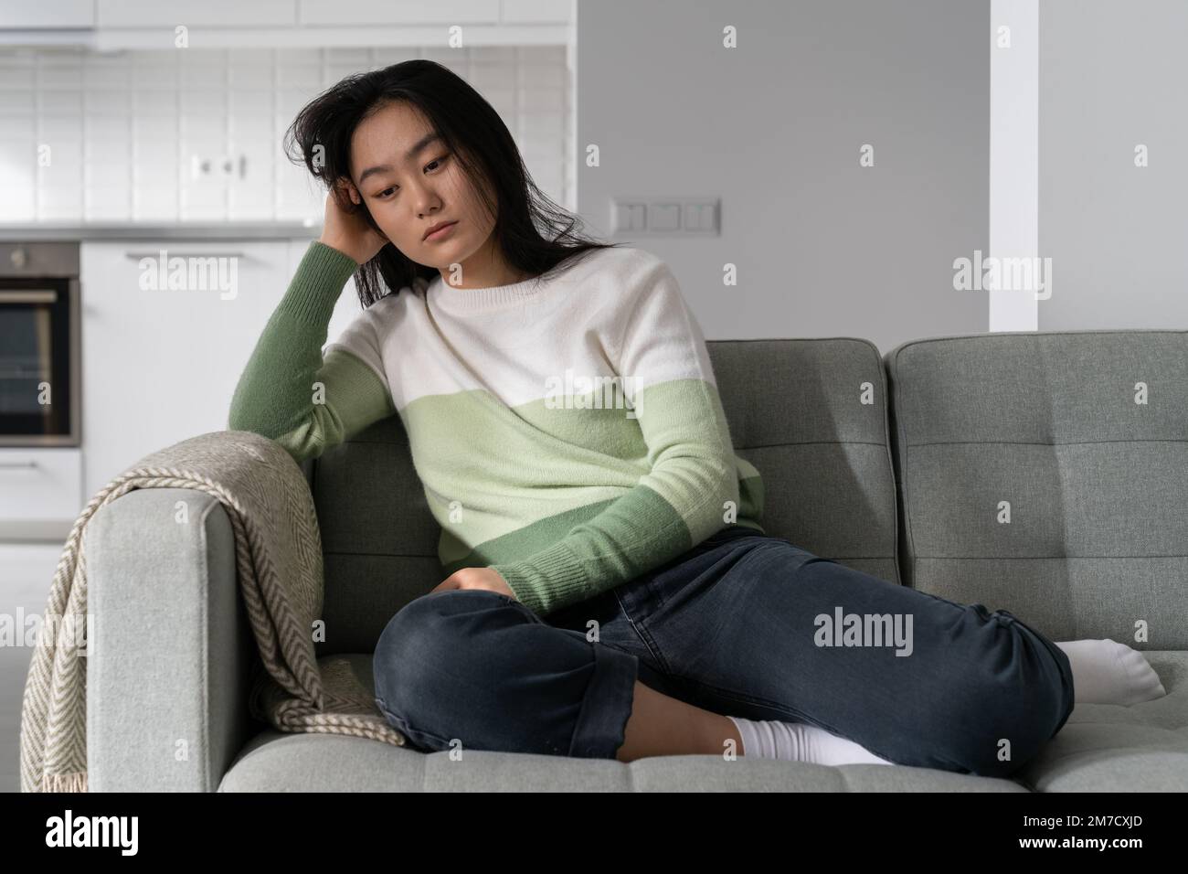 Sad annoyed Chinese woman sits on sofa and suffering depression after ...