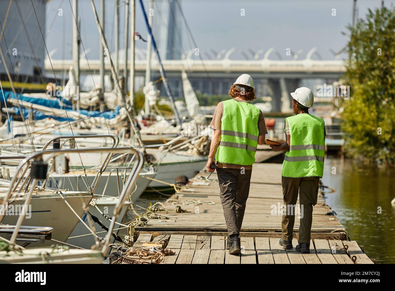 Full length back view of two workers wearing hardhats while walking on ...