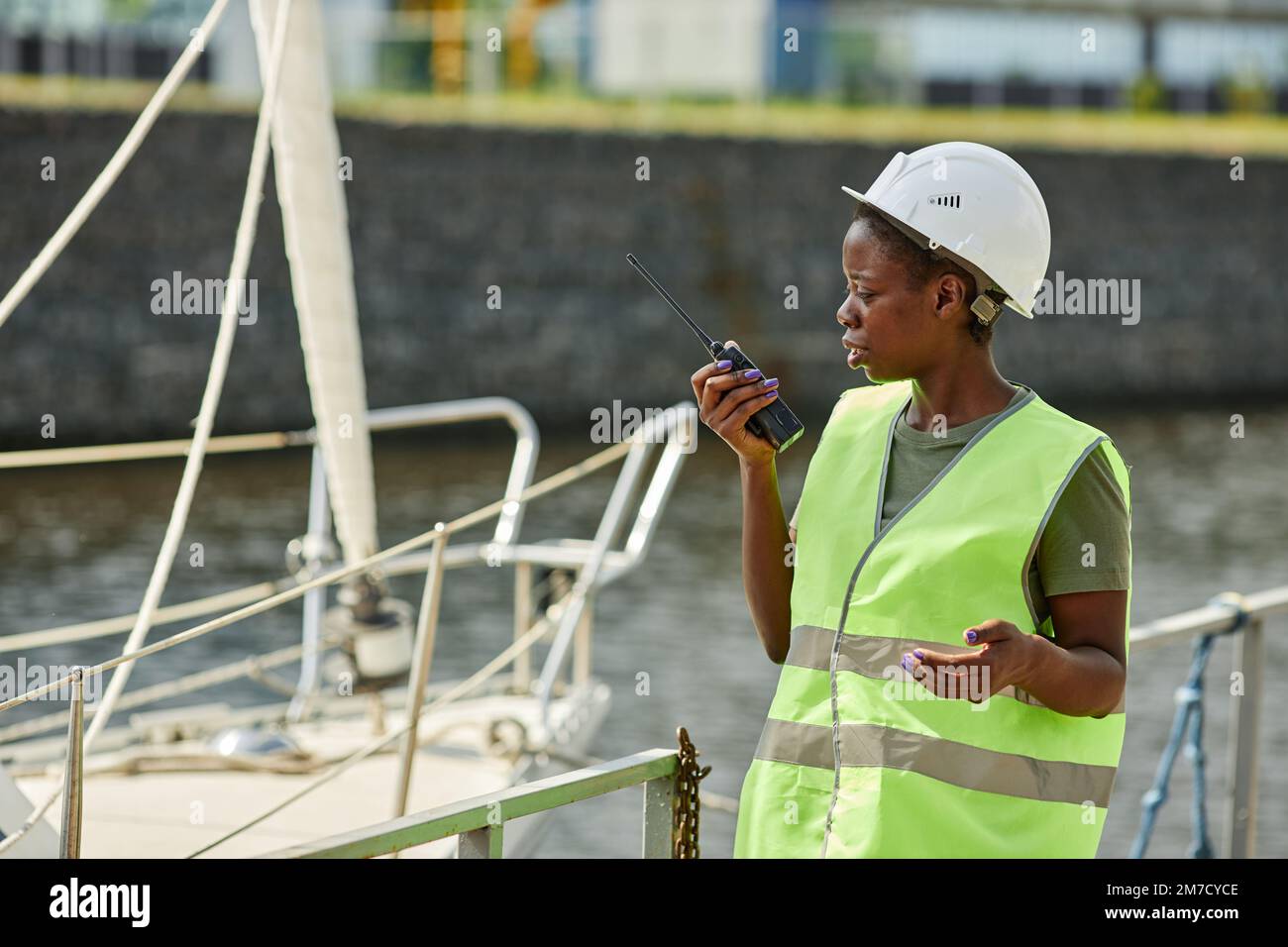 Side view portrait of black young woman speaking to radio while working in yacht docks outdoors ...