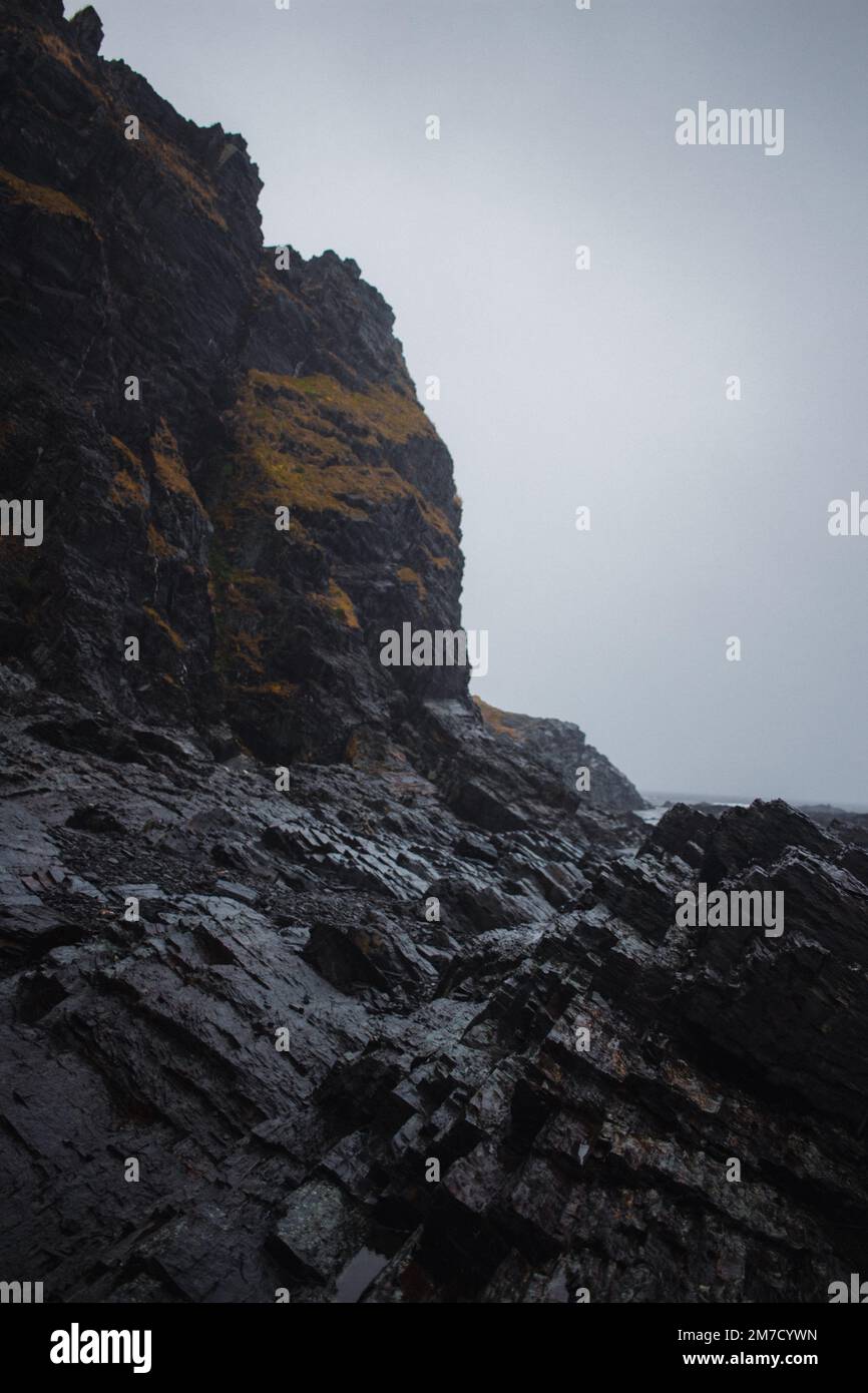 A rocky cliff on a coast by a river with misty sky on the horizon in ...