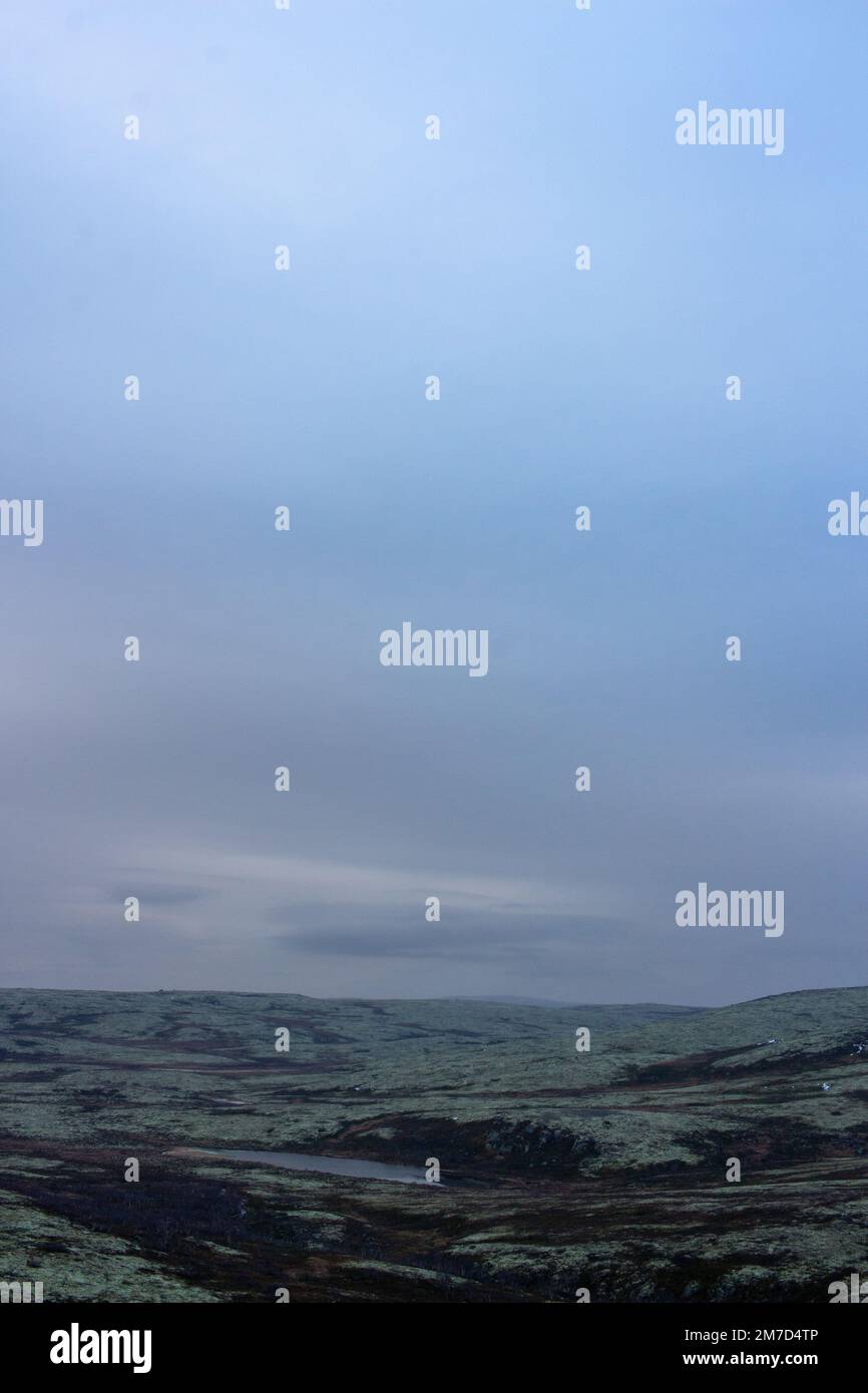 A vertical shot of rocky ground with small pond under blue cloudy sky ...