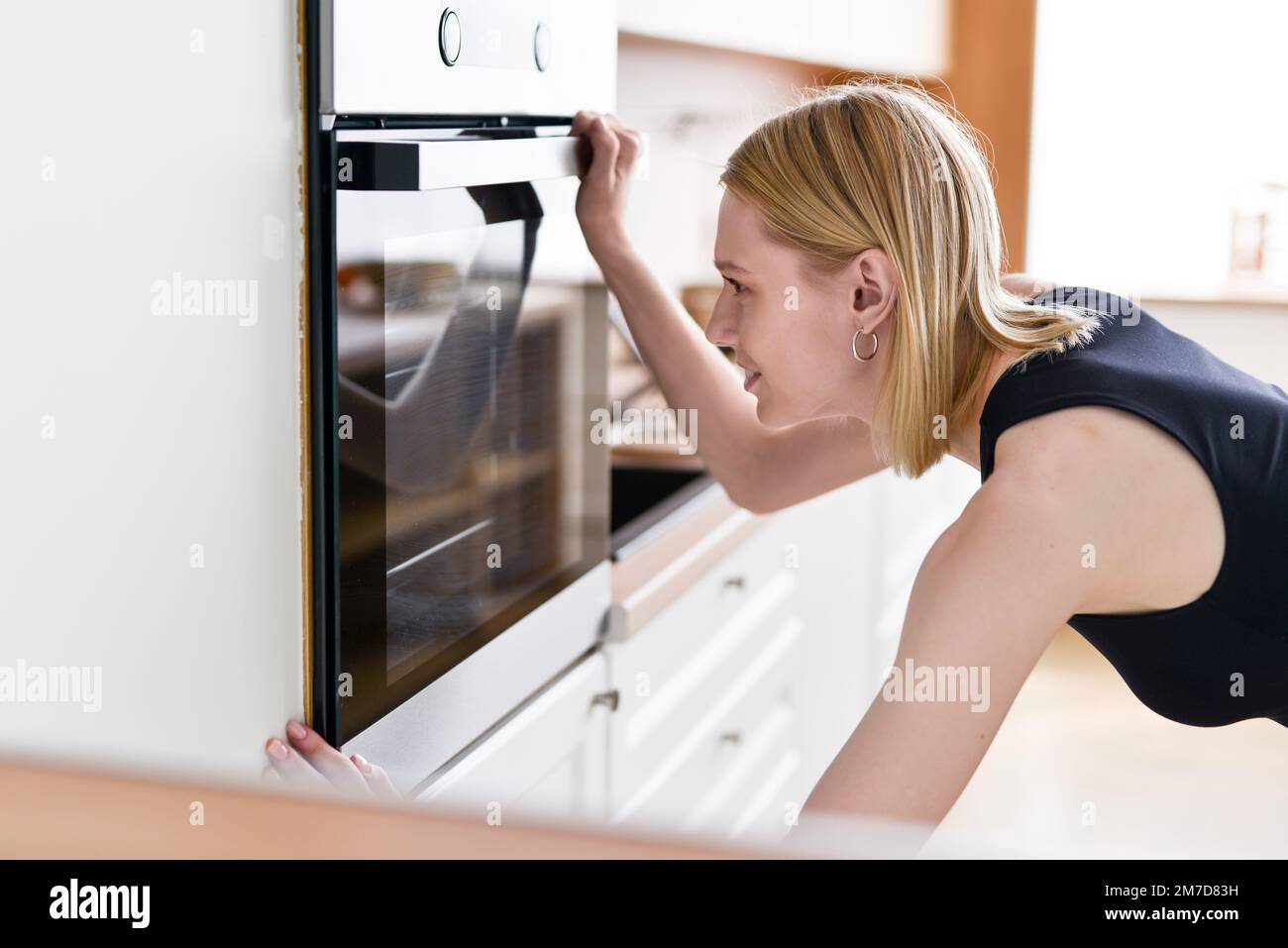 Woman bakes food in oven and looks inside through glass Stock Photo - Alamy