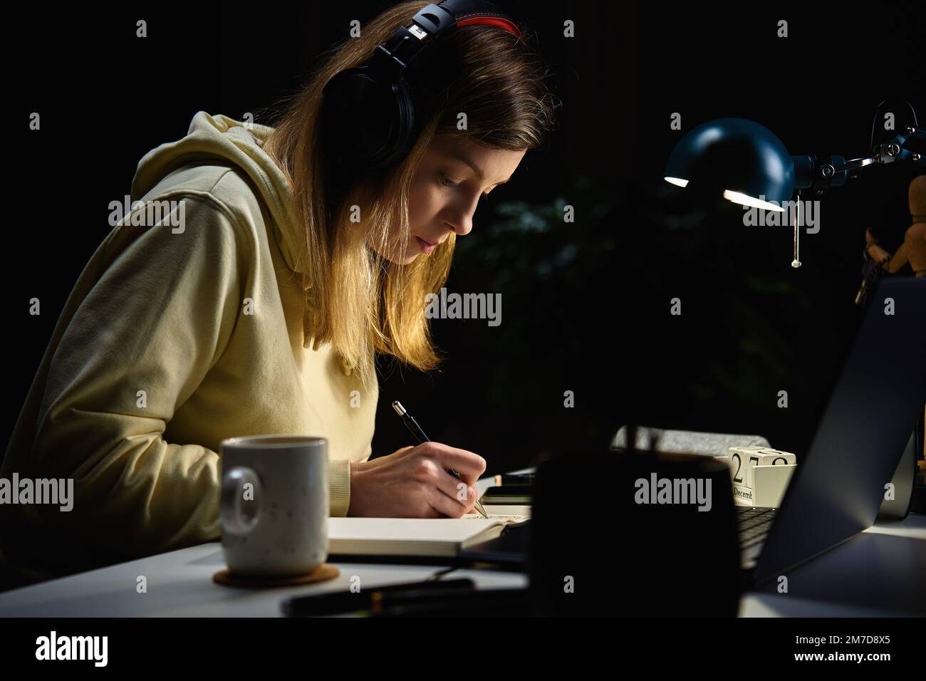 Female sudent wearing headphones studying at night room, using laptop ...