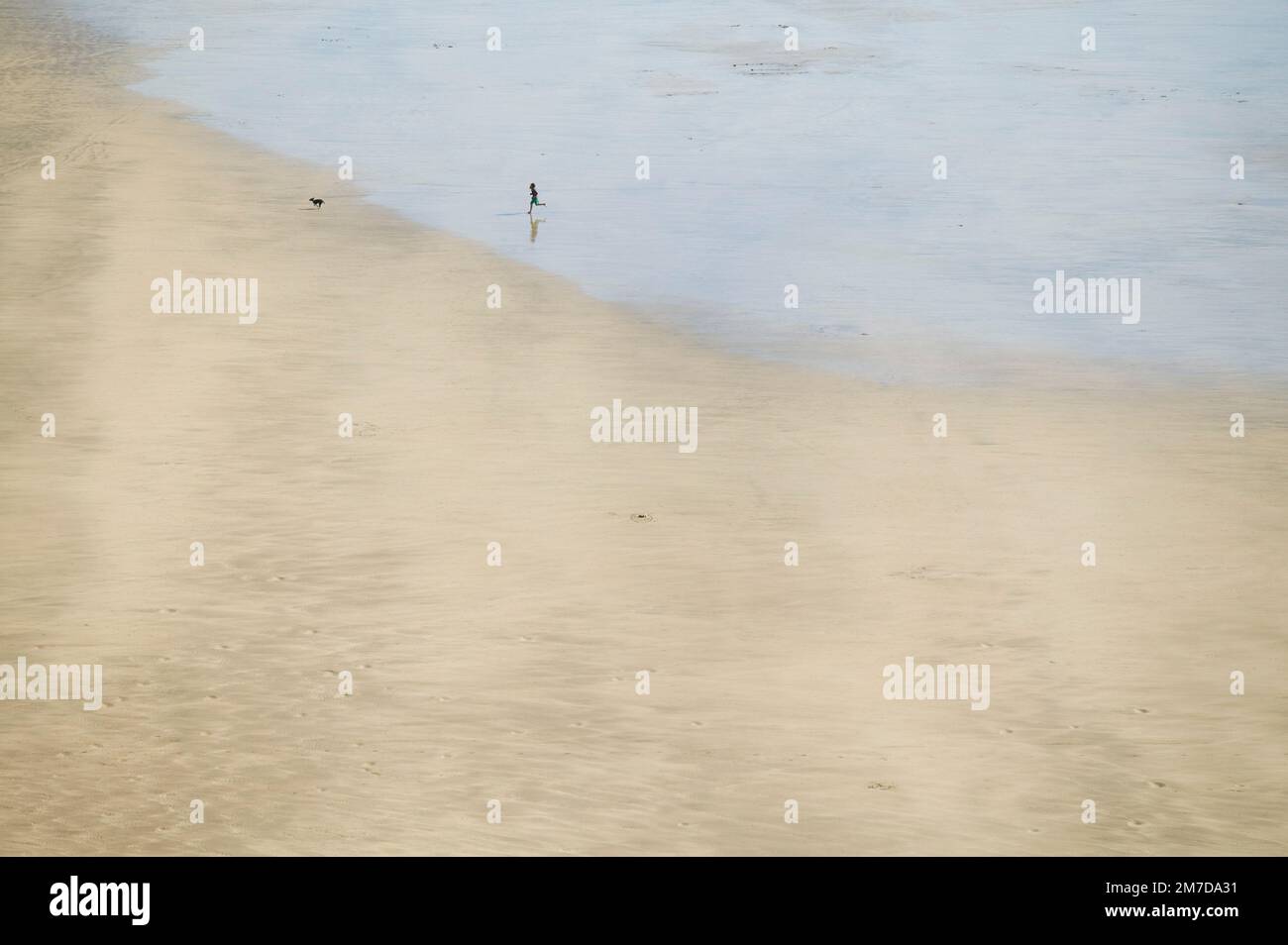 A tiny figure with shadow is silhouetted on the sand of a vast empty ...