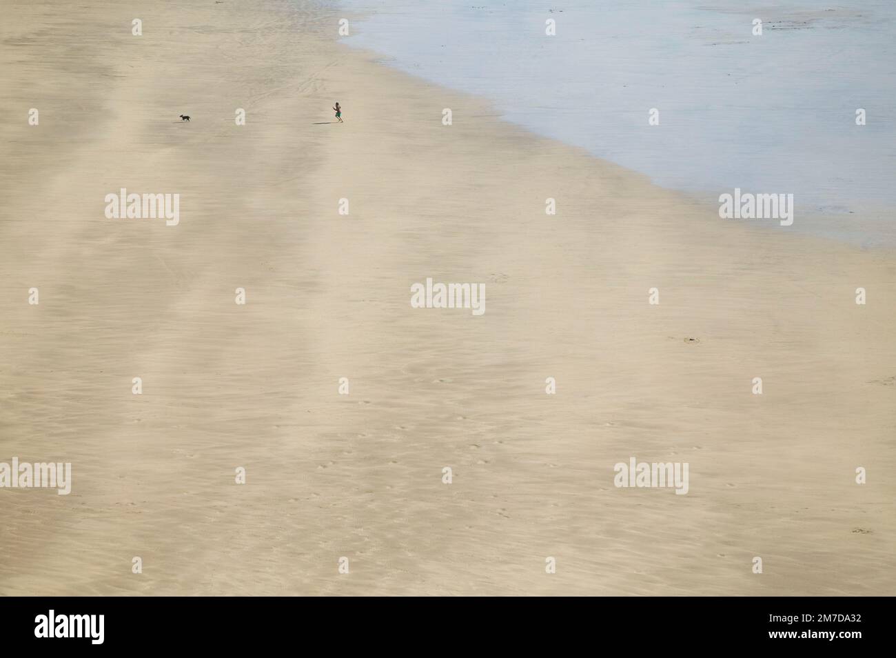A tiny figure with shadow is silhouetted on the sand of a vast empty ...