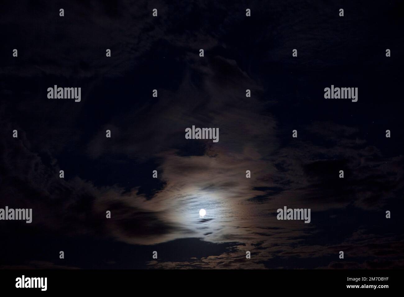 The moon half hidden by passing cluds lights them from behind producing ...