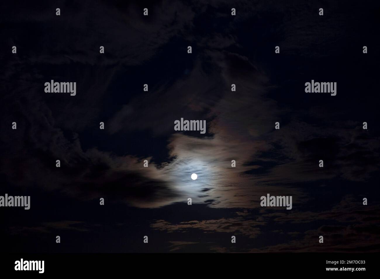 The moon half hidden by passing cluds lights them from behind producing ...