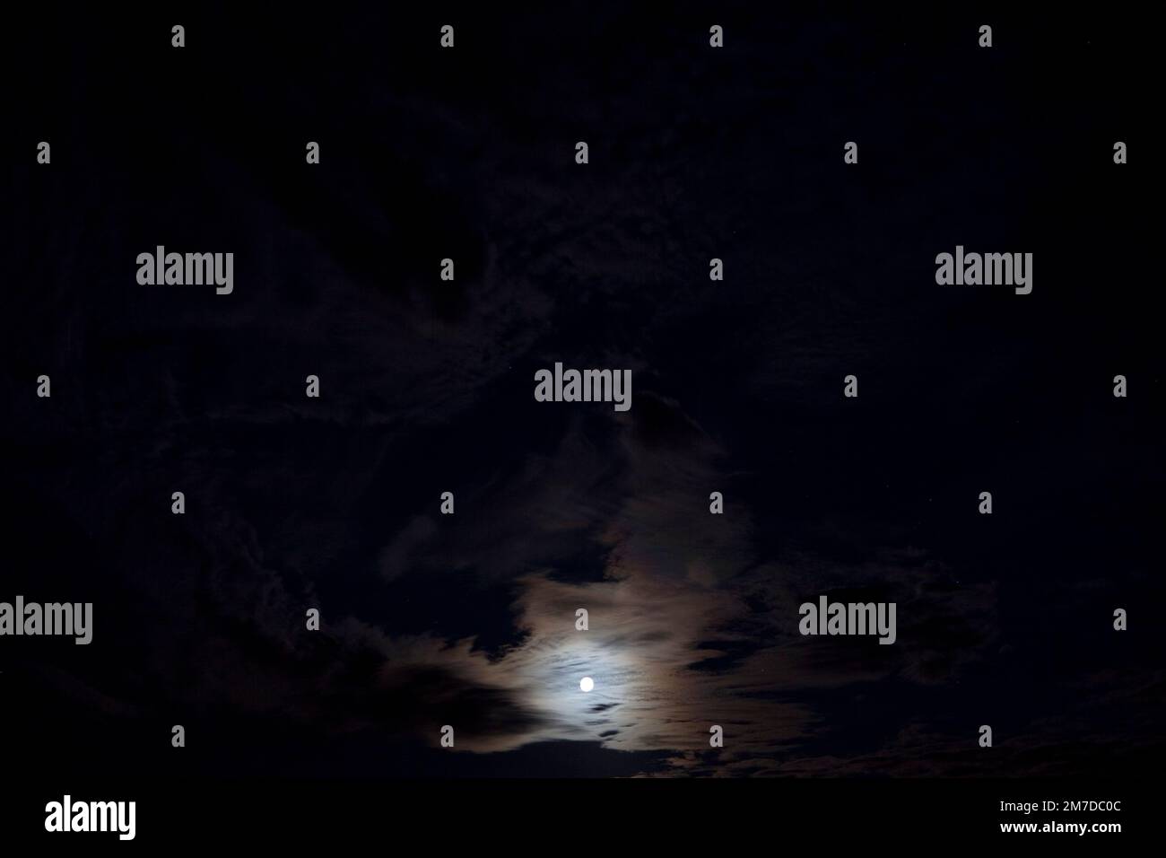 The moon half hidden by passing cluds lights them from behind producing ...