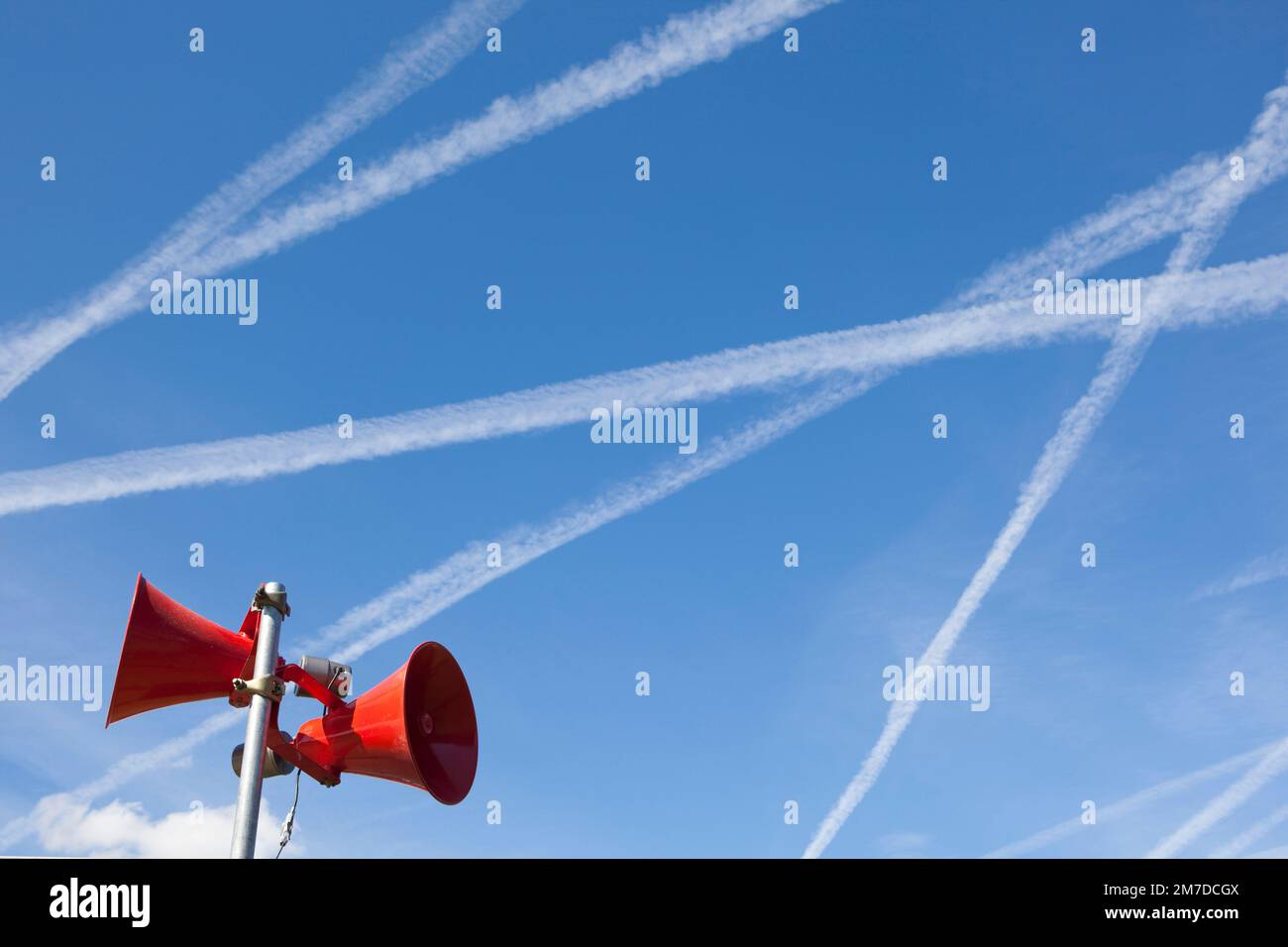 A pair of red loudspeakers or horns set against a blue sky and used to ...