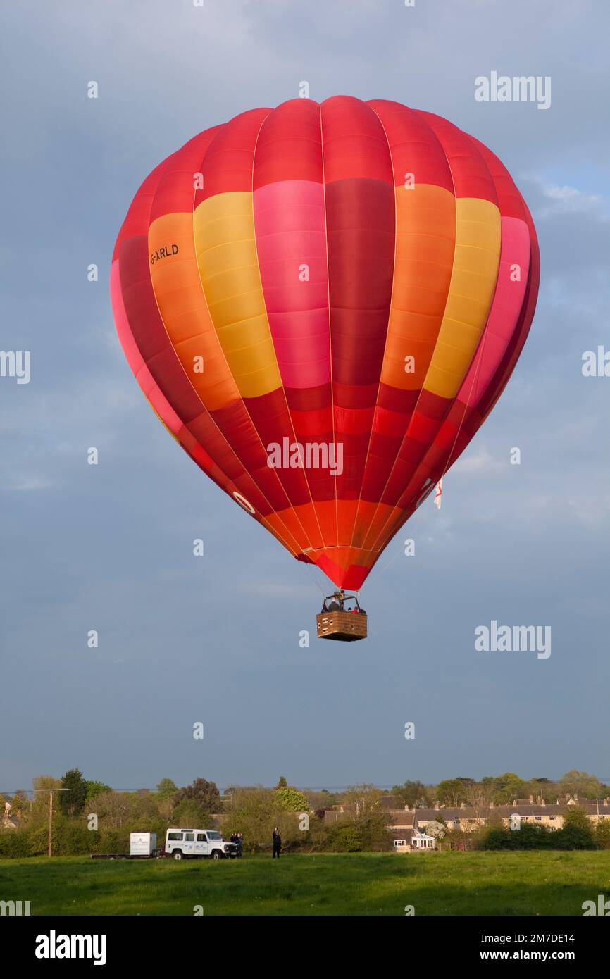 A bright red hot air ballon lifts off from a field on the Cotswolds ...