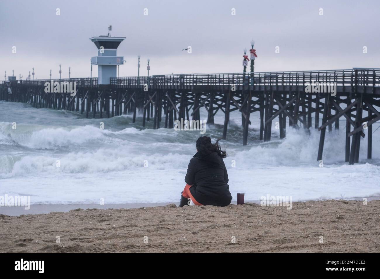 A woman siting on the storm surge protection dune watches the waves ...