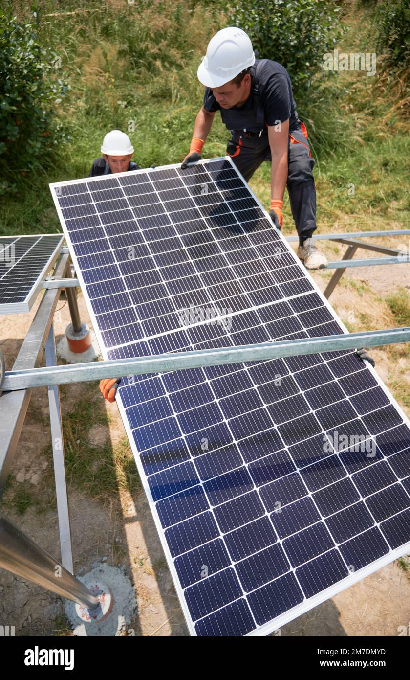Two men in safety helmets installing solar modules on metal ...