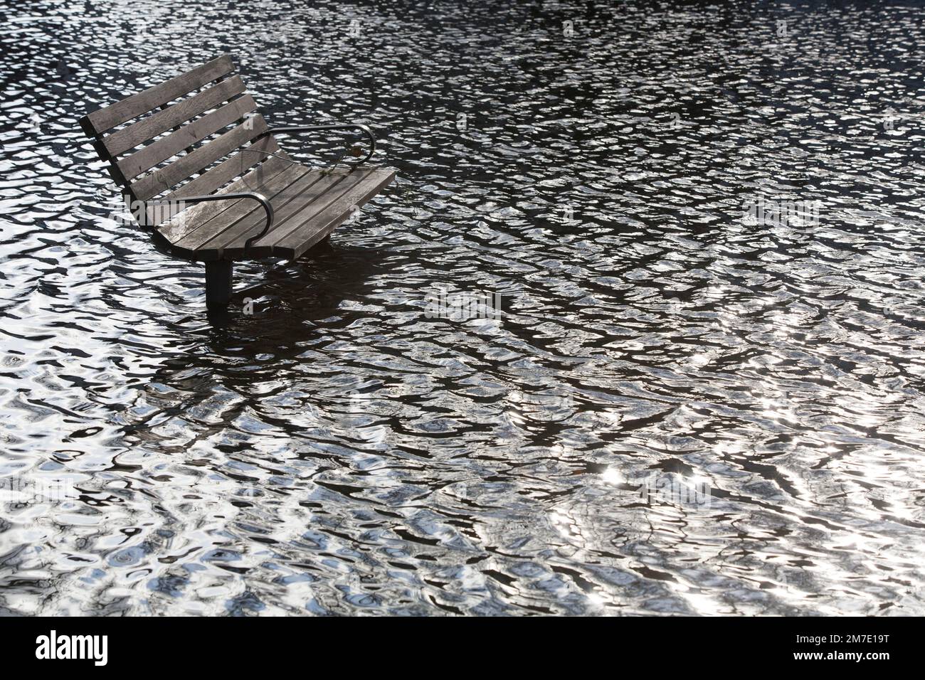 A wooden park bench in a flooded field indicating the change in wether ...