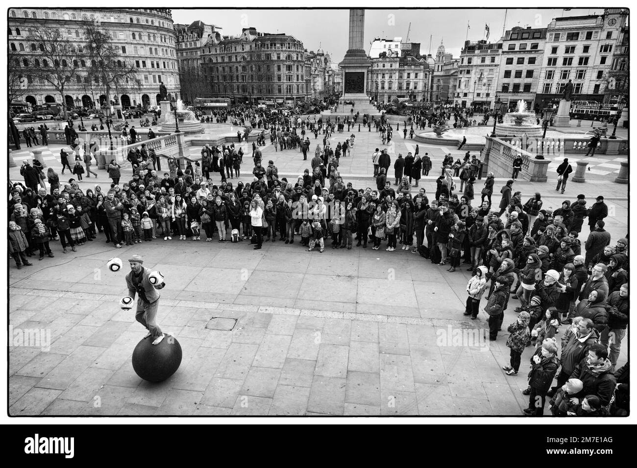 A street entertainer and juggler standing on a large ball entertains ...