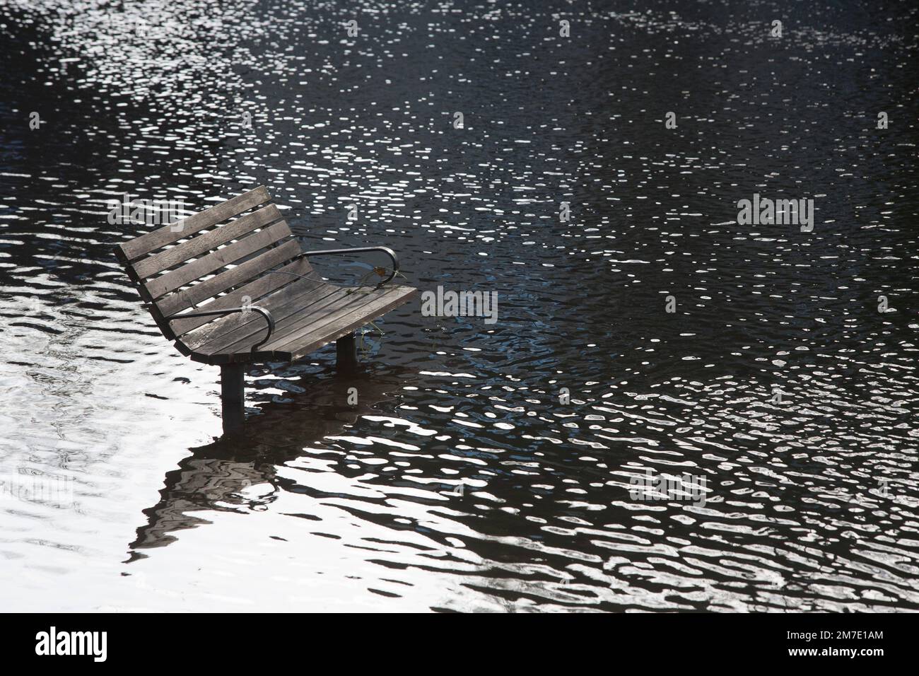 A wooden park bench in a flooded field indicating the change in wether ...