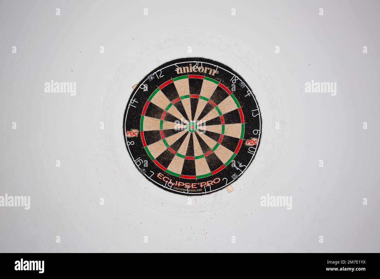 A dartboard attached to a white wall with marks where darts ahve missed ...