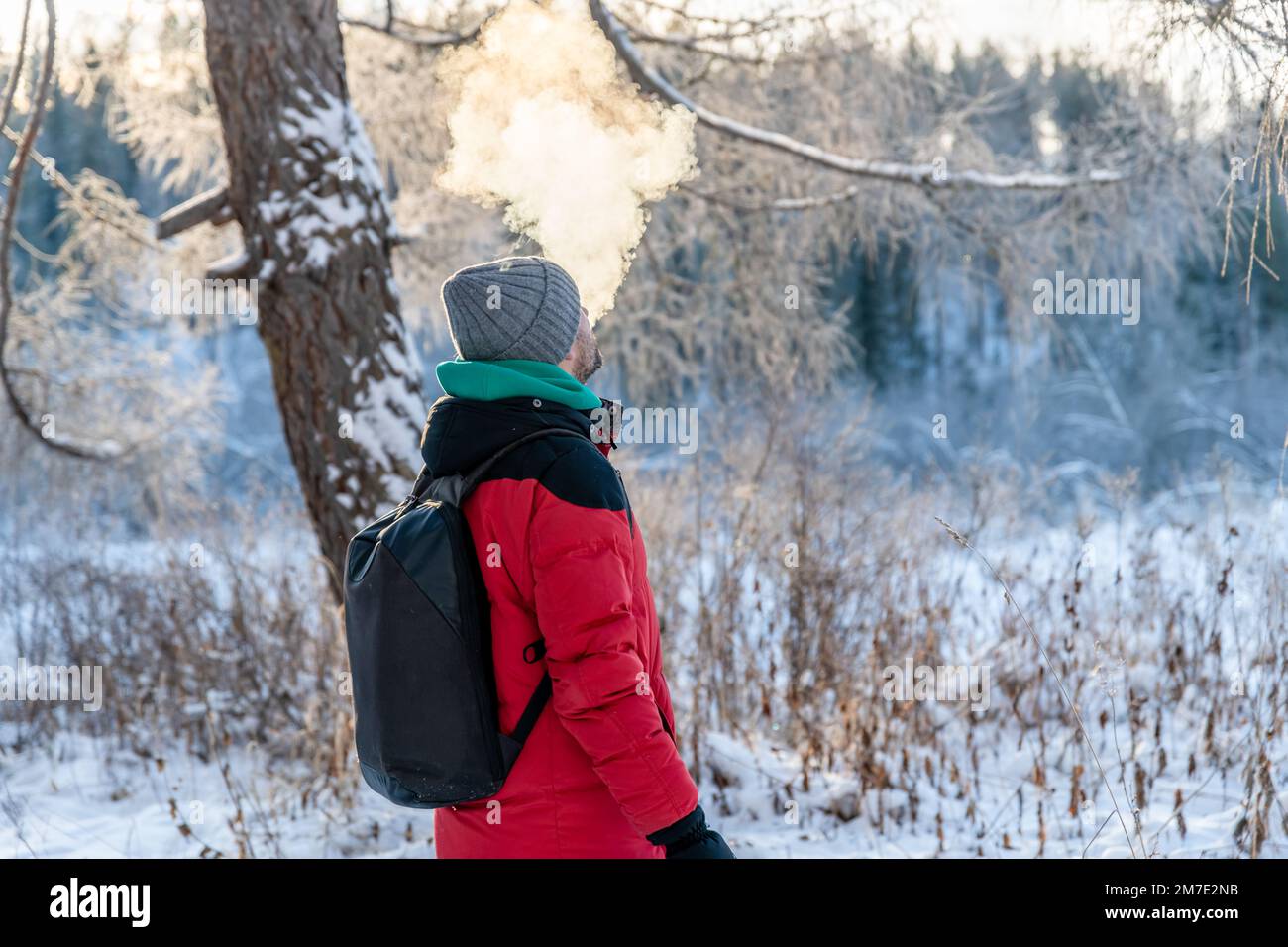 a man in the winter in the cold exhales a cloud of steam, smoke ...