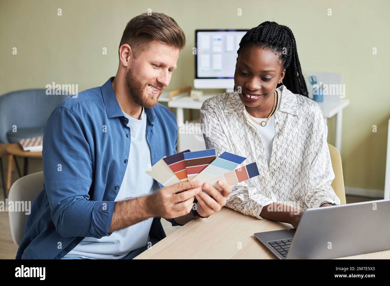 Portrait of two smiling young designers looking at color swatches while ...