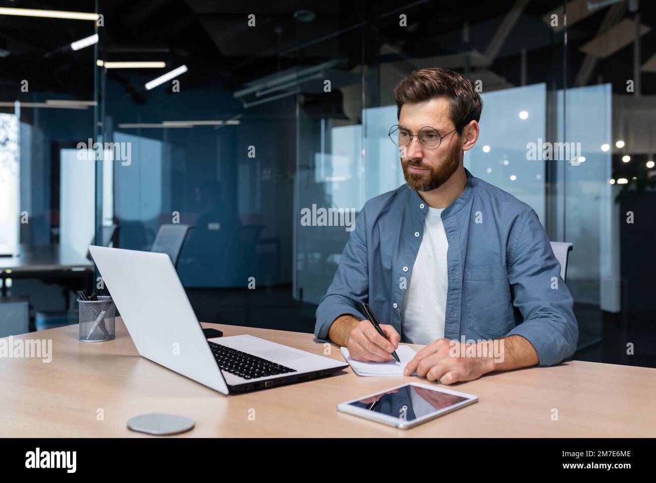 Serious businessman is writing down information studying online while ...