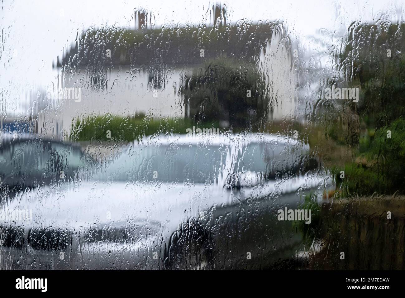 Looking out of a window covered in rain during a storm at cars parked ...