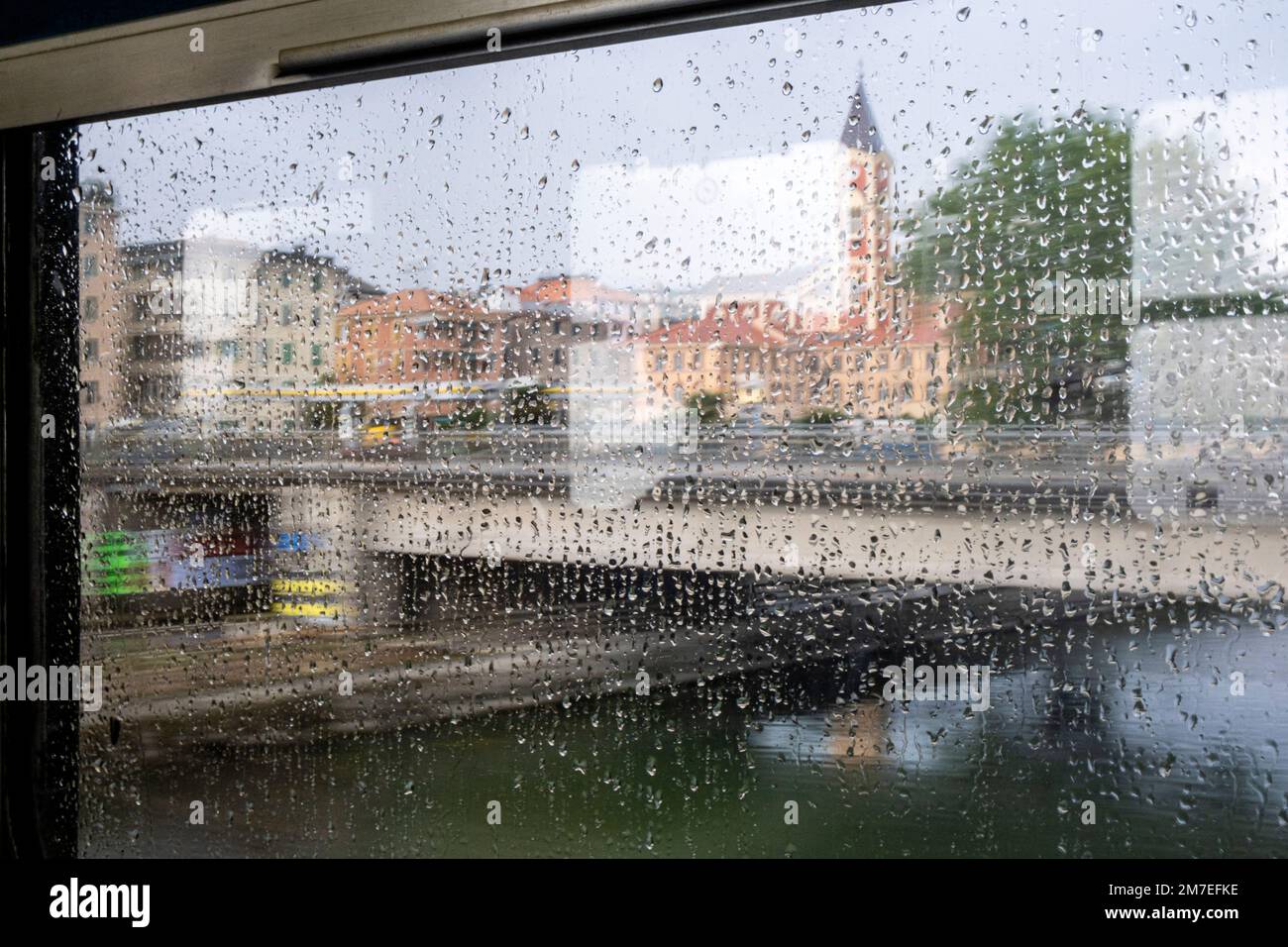 View from a train window of a city street scene obscured by rain on the ...