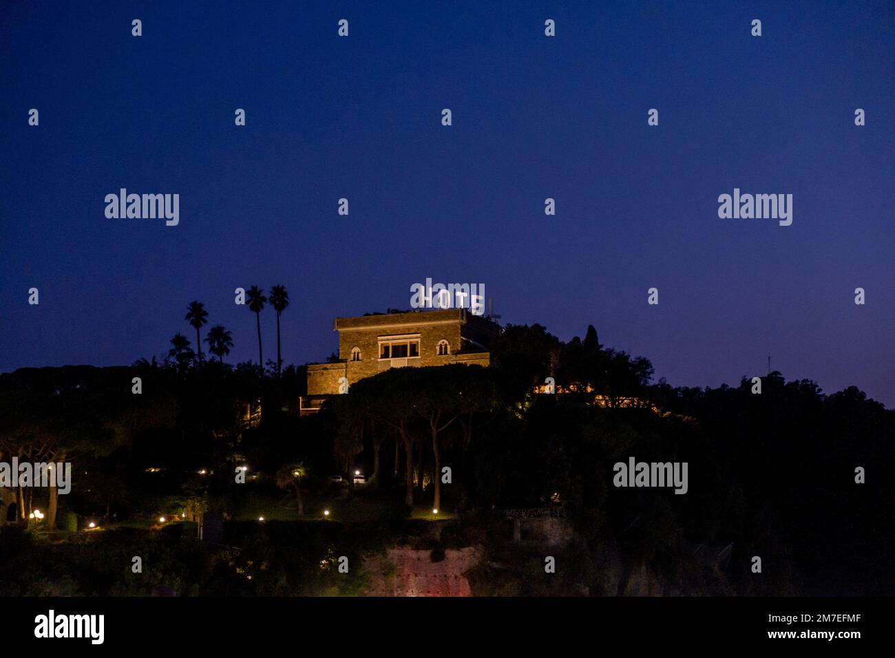 An old hotel on the top of a hill with brightly lit sign with the L ...