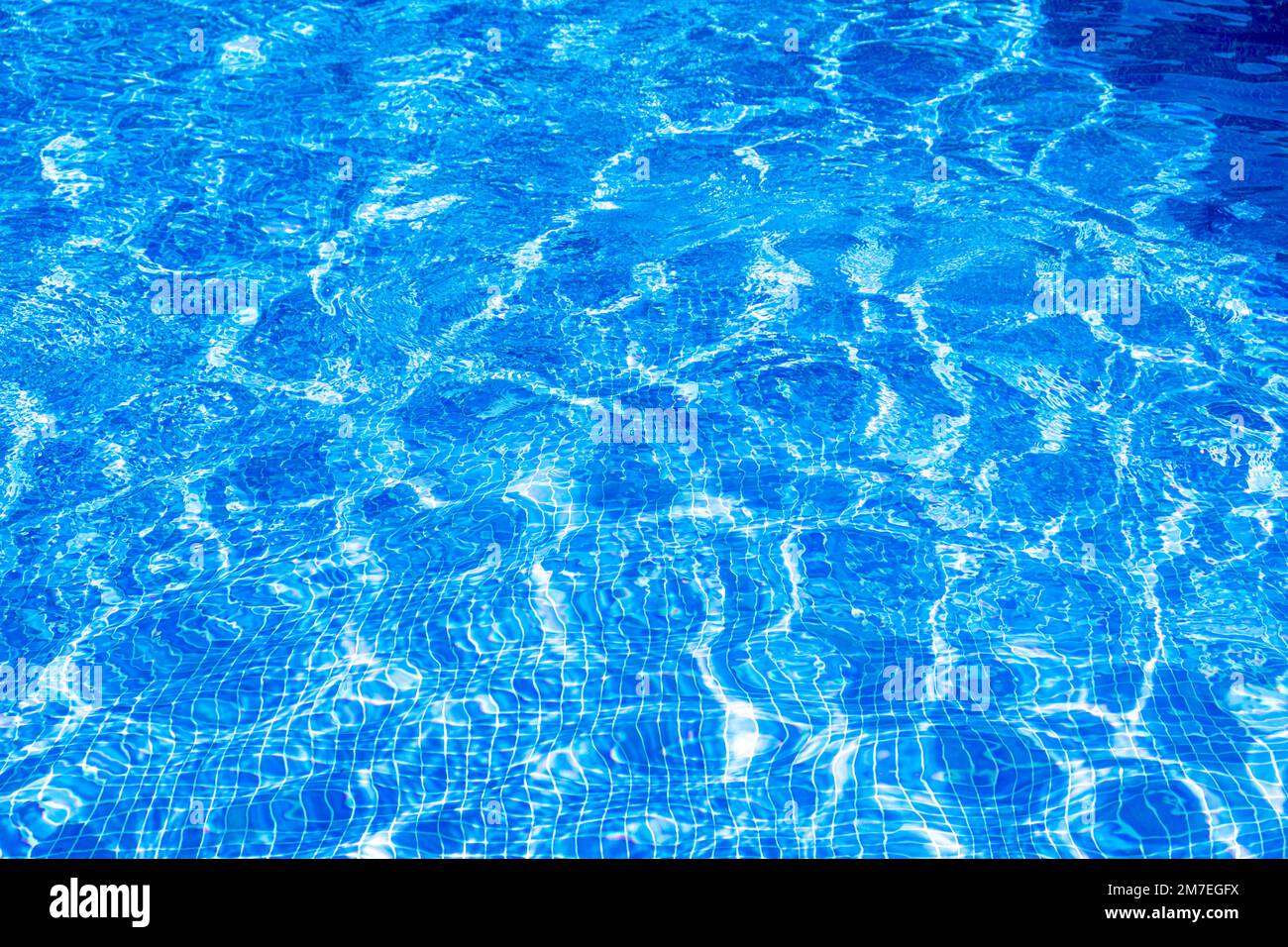 Sunlight reflects on the ripples of the surface of an outdoor swimming ...