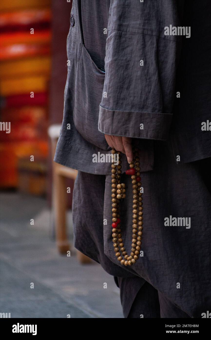 A vertical shot fo a monk with gray clothes holding a rosary Stock ...