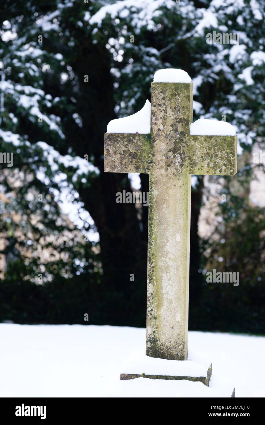 A stone cross marks the place of a burial in a snow covered graveyard ...