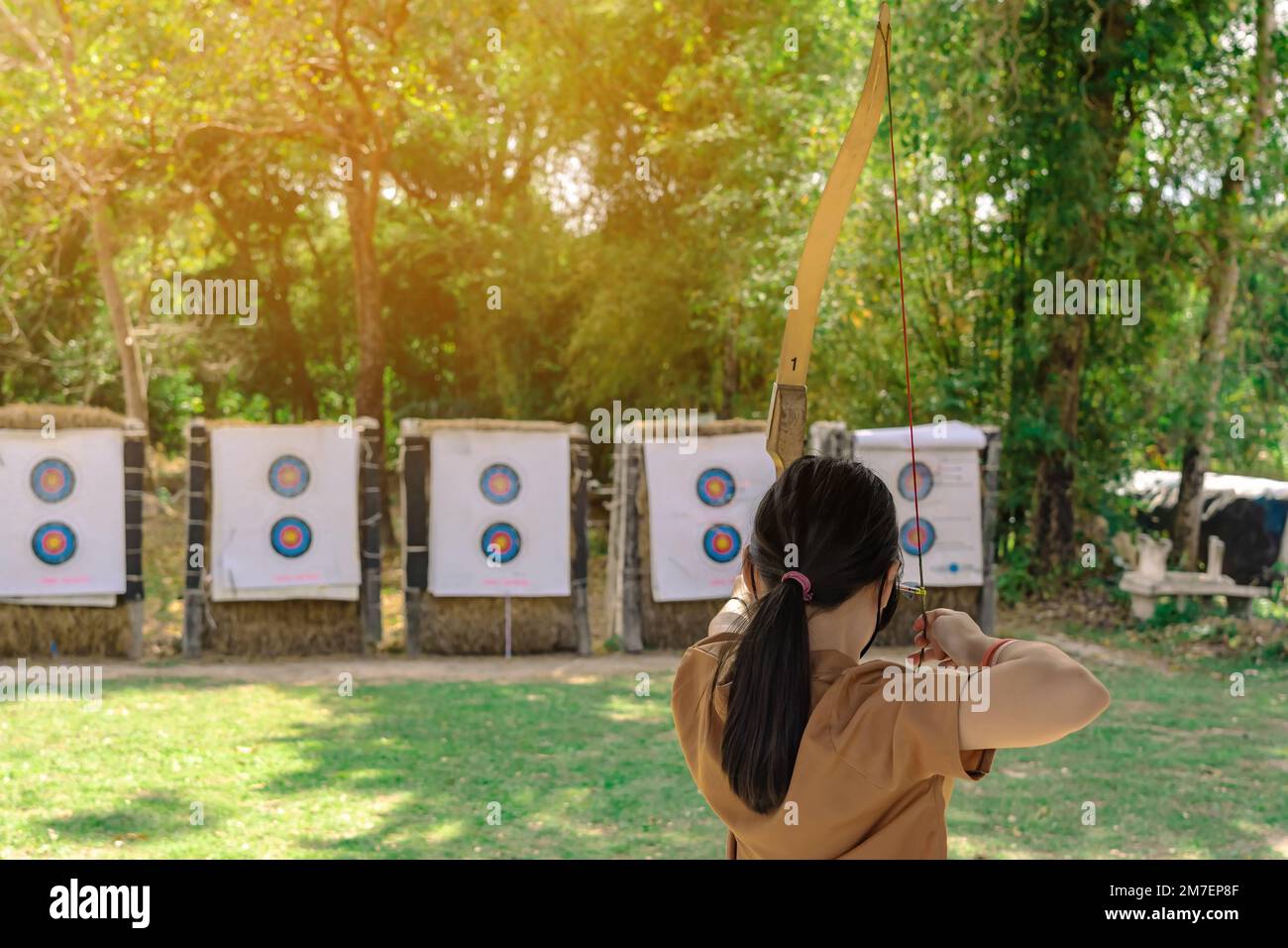 Back view of Asian girl wear face mask aims archery bow and arrow to ...