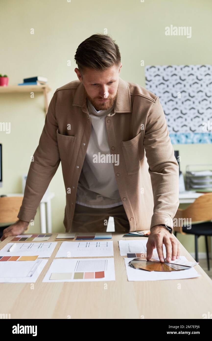 Vertical portrait of male designer choosing color palette while working ...