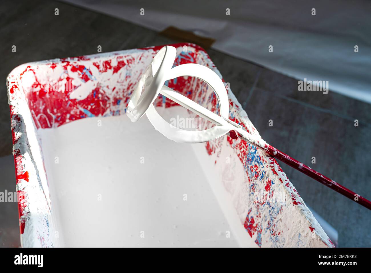 An open plastic bucket with white paint and a stirrer standing on the ...