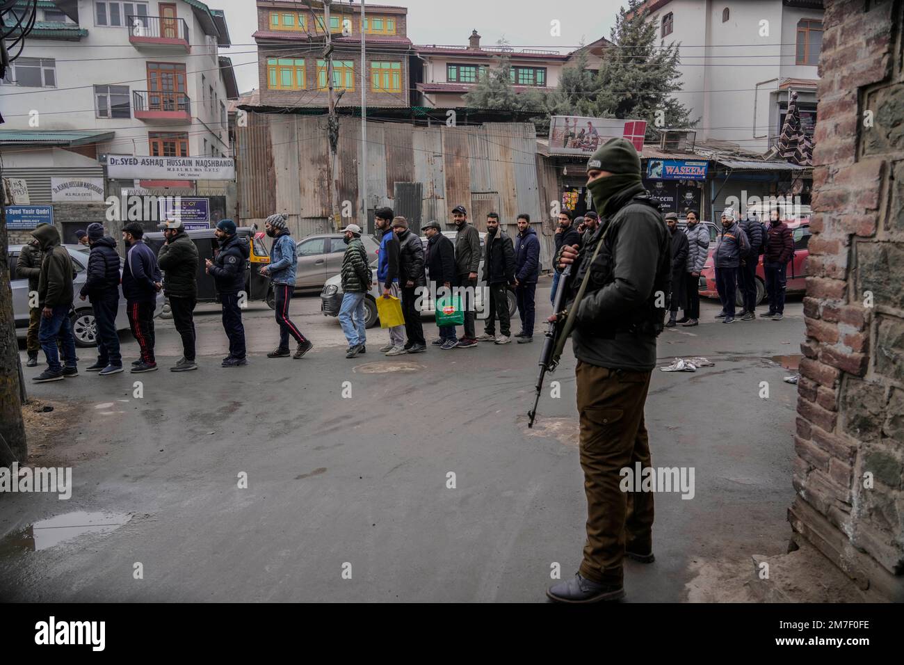 An Indian policeman guards as Kashmiri men stand in a queue during a ...