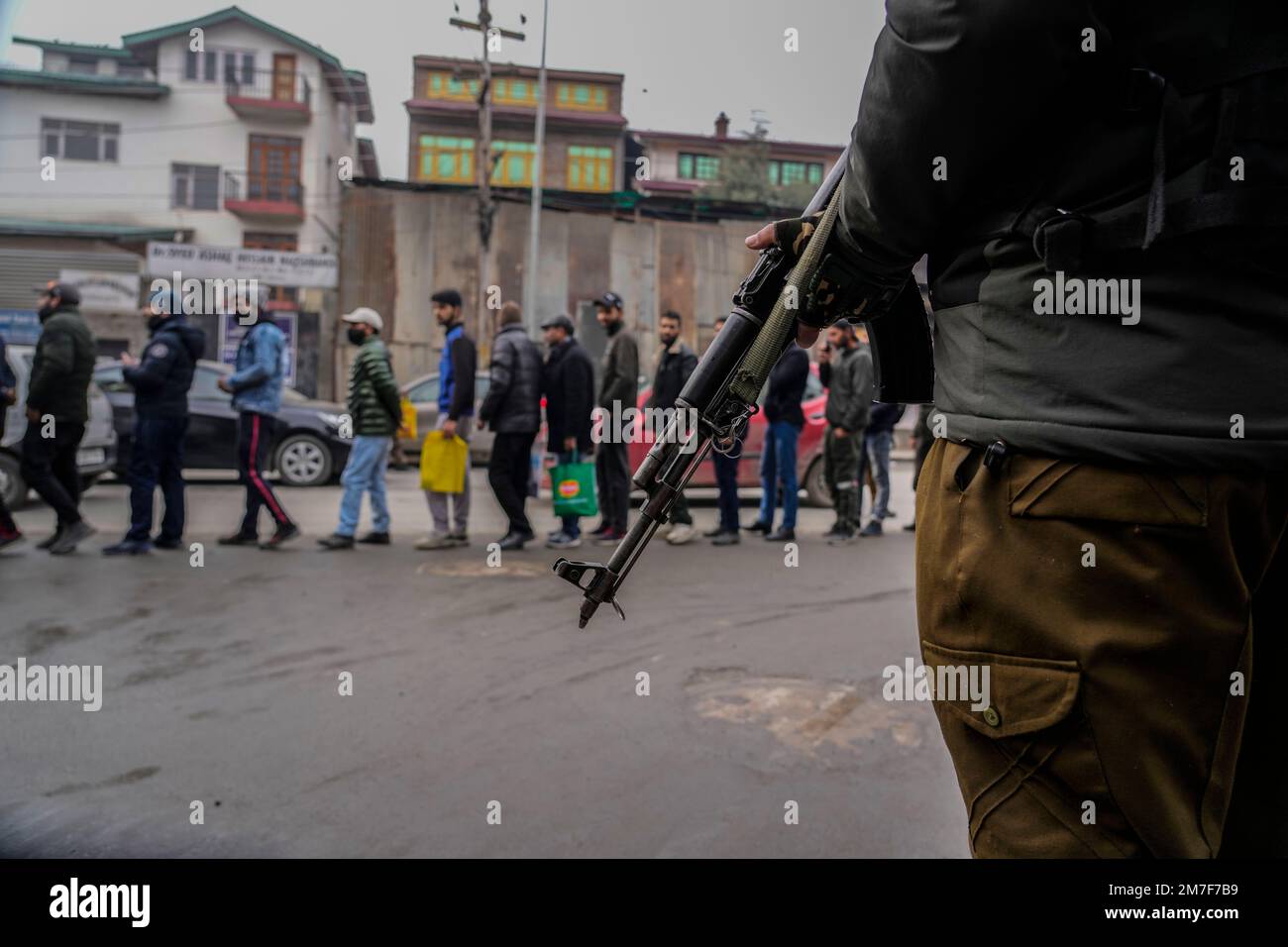 An Indian policeman guards as Kashmiri men stand in a queue during a ...