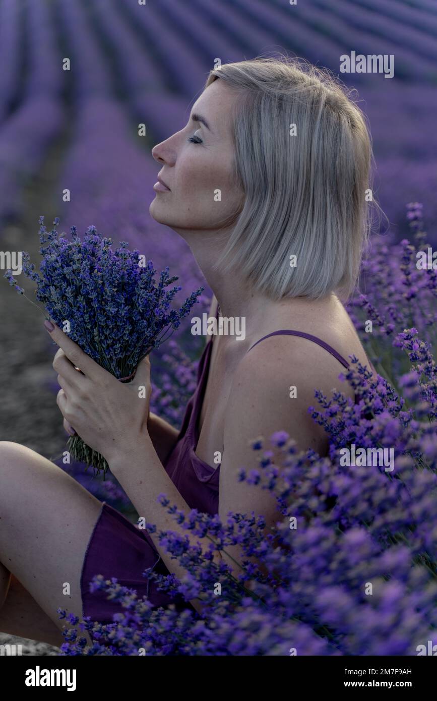 A middle-aged woman sits in a lavender field and enjoys aromatherapy ...