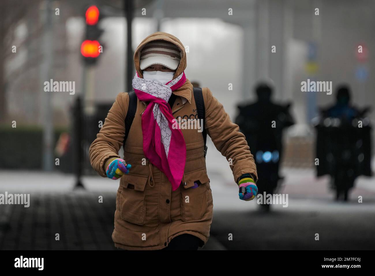 A woman wearing a face mask and covered with hood runs across a street ...