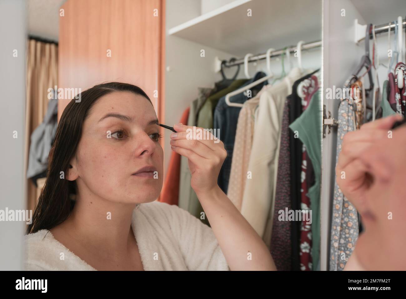 Beautiful Hispanic woman in a white bathrobe applying black makeup to ...