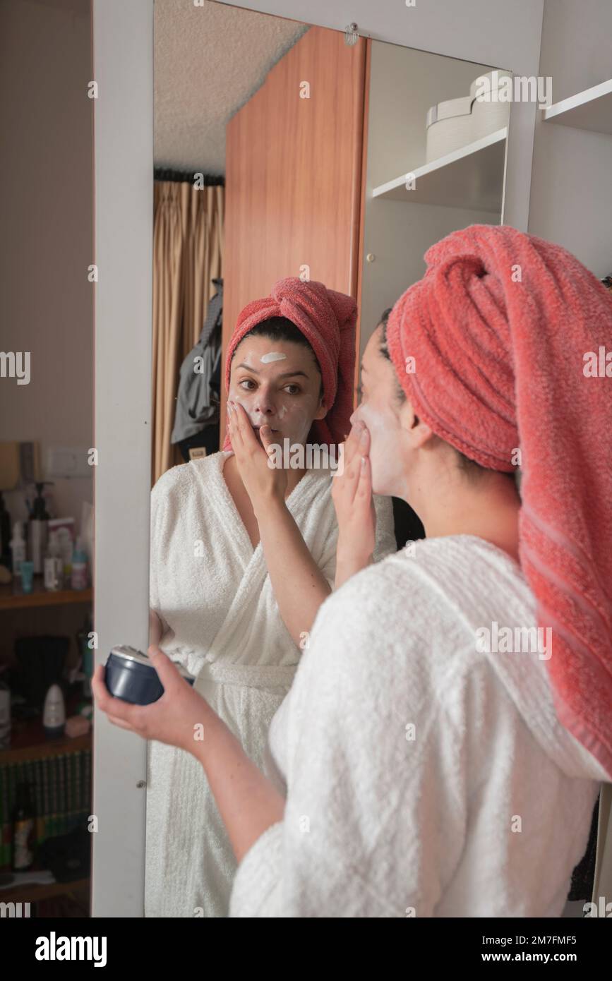 Beautiful Hispanic woman in a white bathrobe and red towel in her hair ...